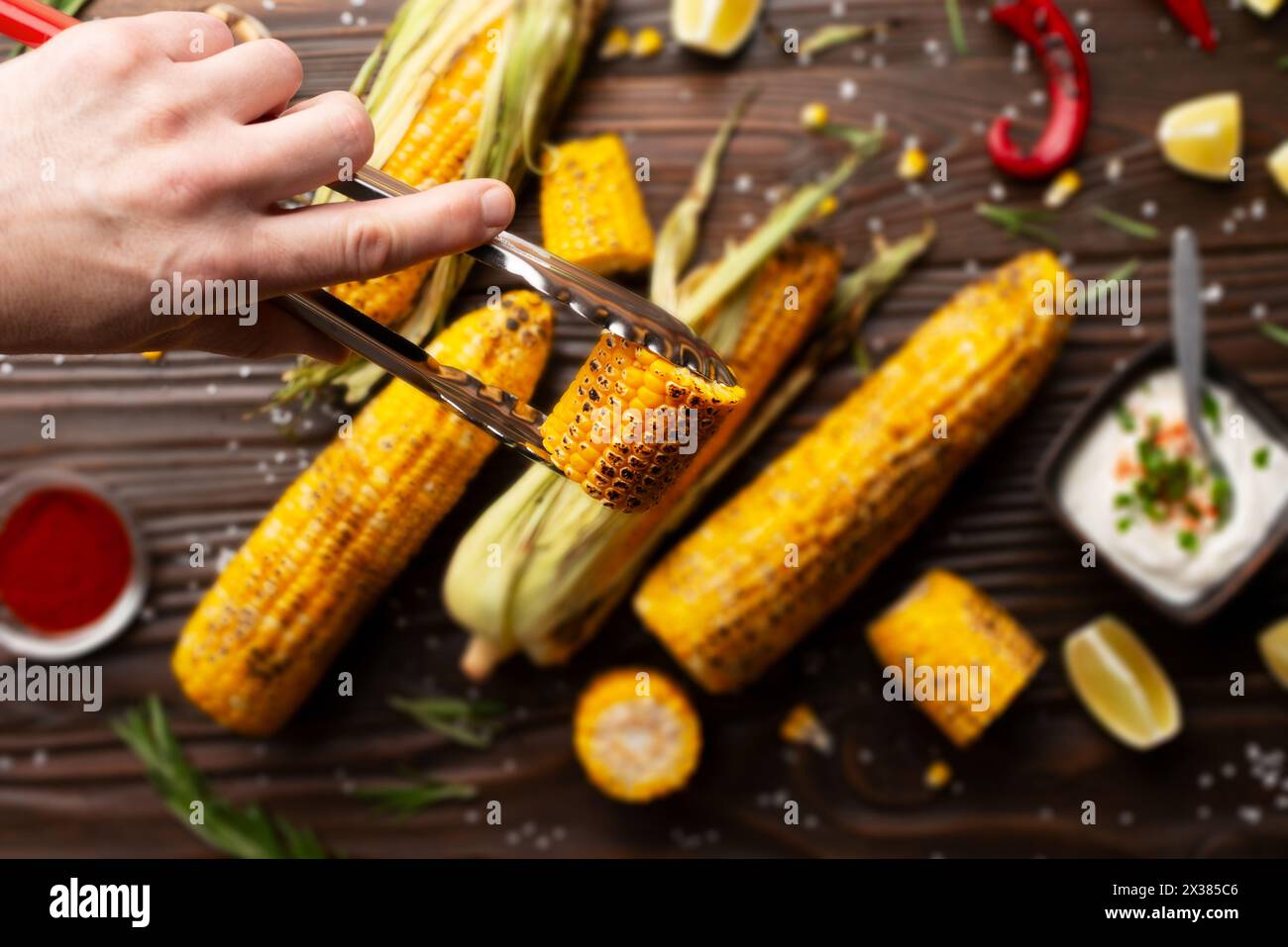 Kitchen tongs with grilled corn on the cob pieces in caucasian hands on ...