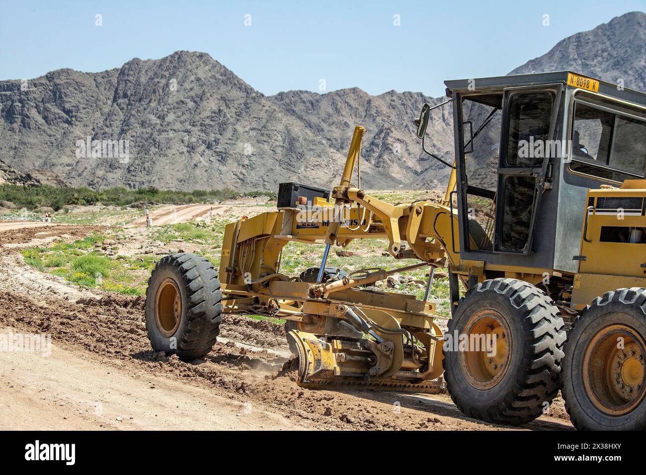 The bright yellow grader scraping the road along the Orange River ...