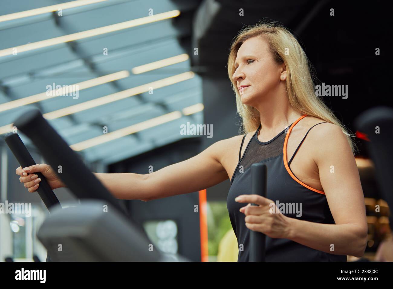 Mature woman in workout gear using an elliptical trainer, focused on ...
