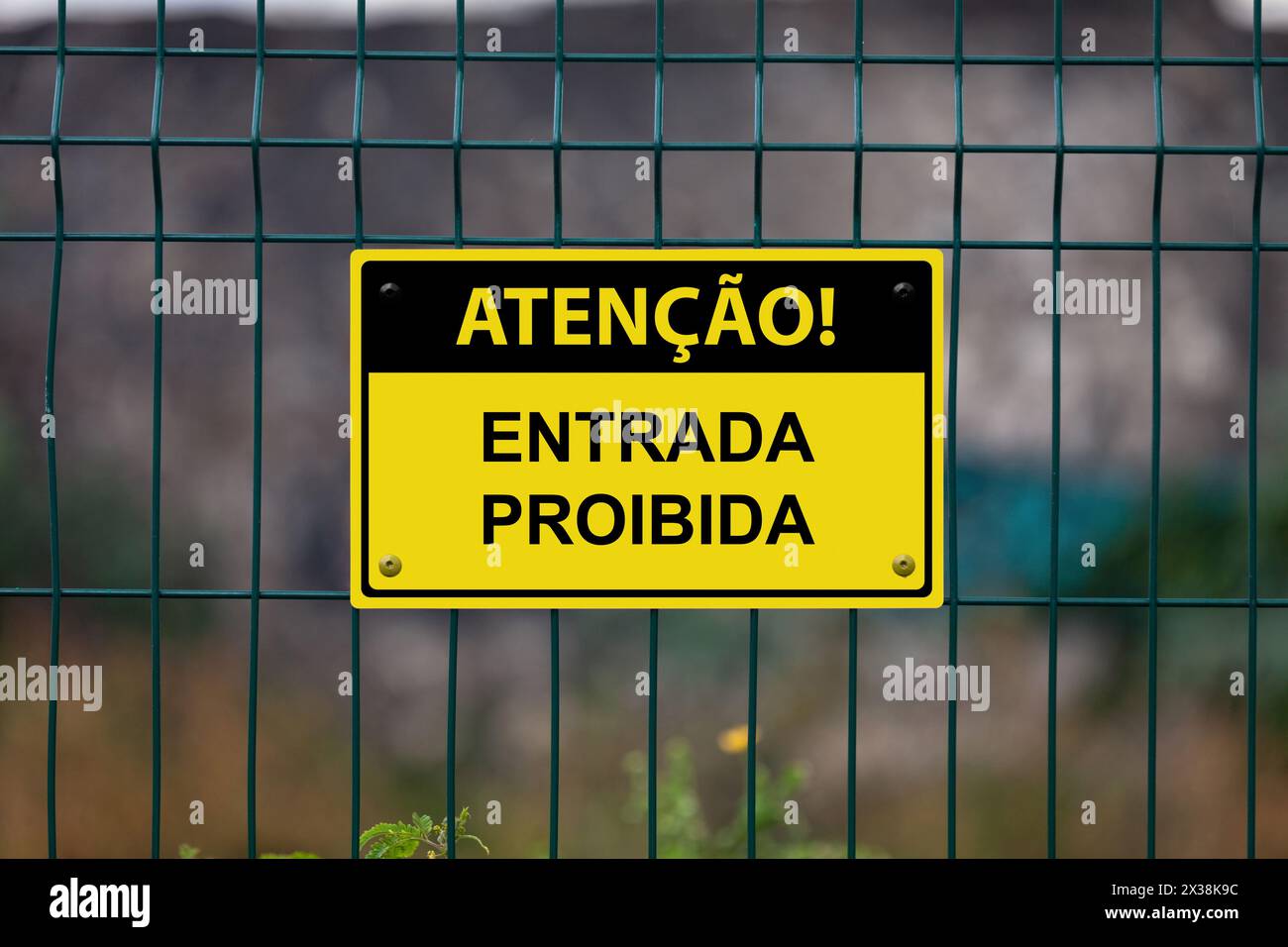Yellow warning sign on a fence stating in portuguese: "Atenção ...