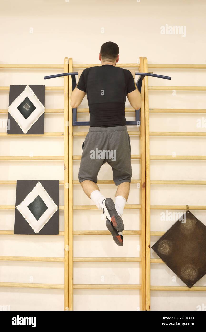 Young man in black pull-up on horizontal bar in gym, back view Stock ...