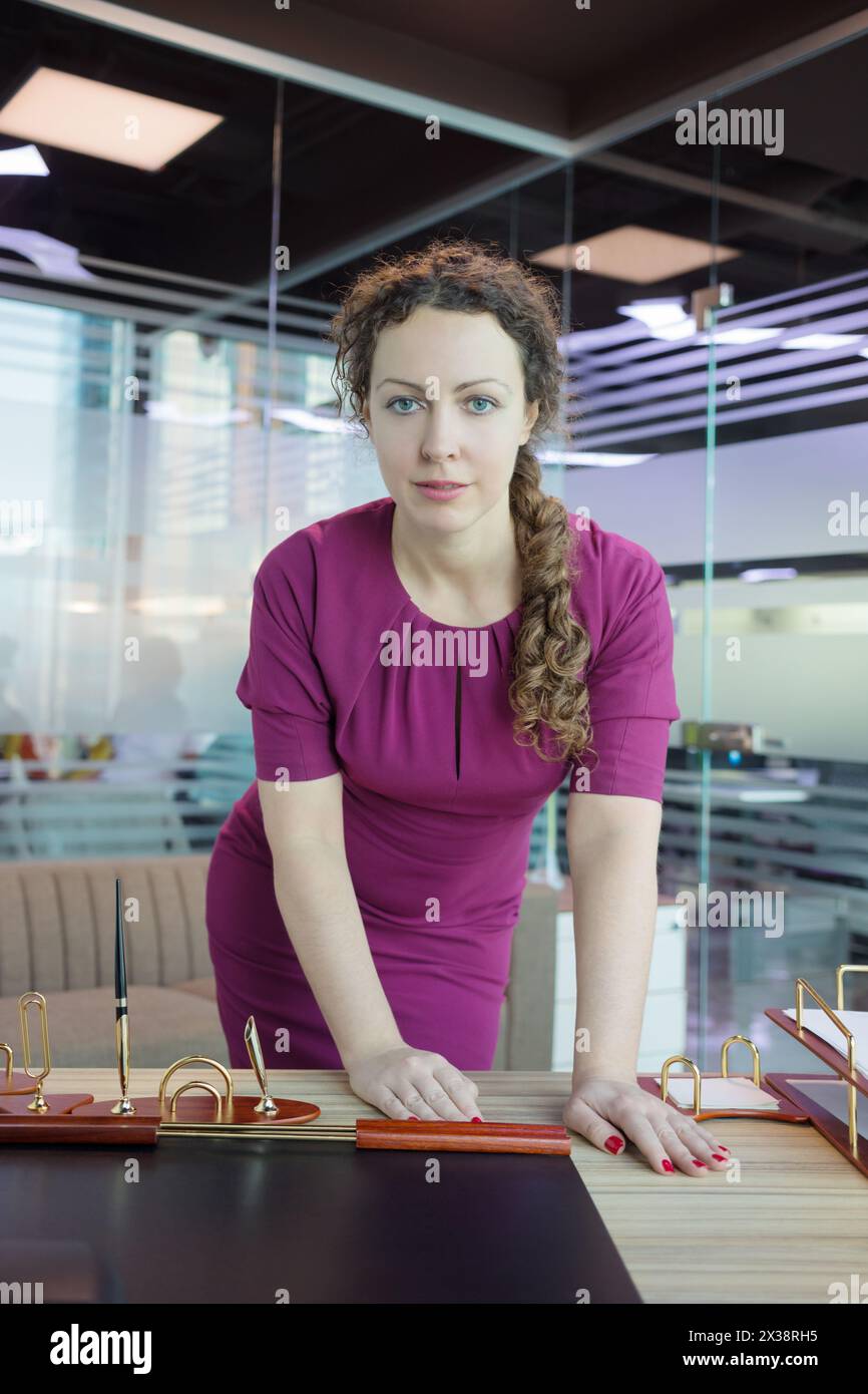 Beautiful woman in dress poses in modern office with table and glass ...