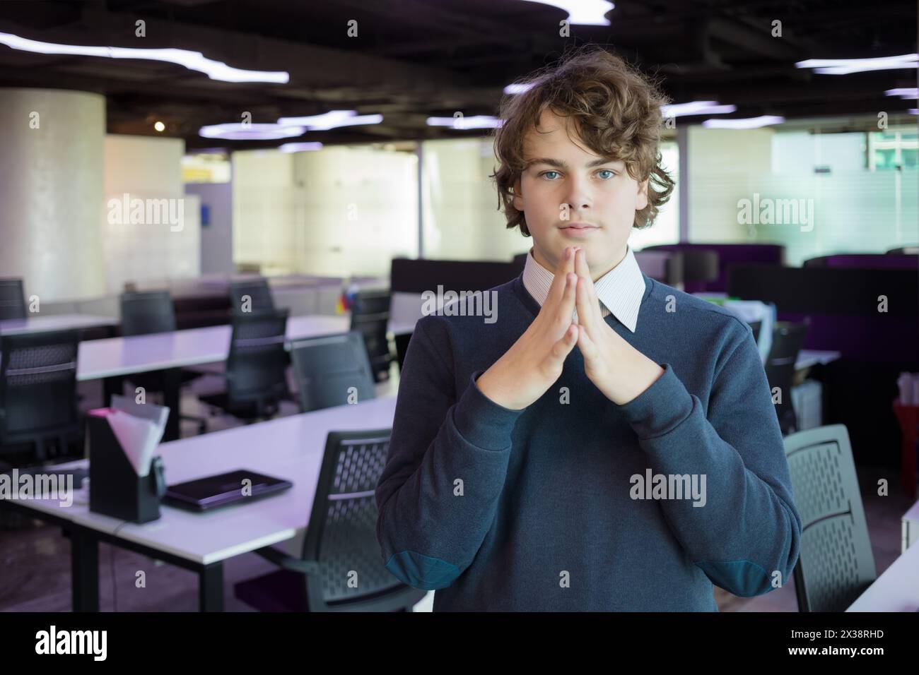 Handsome teenager poses with folded hands in modern office with many ...
