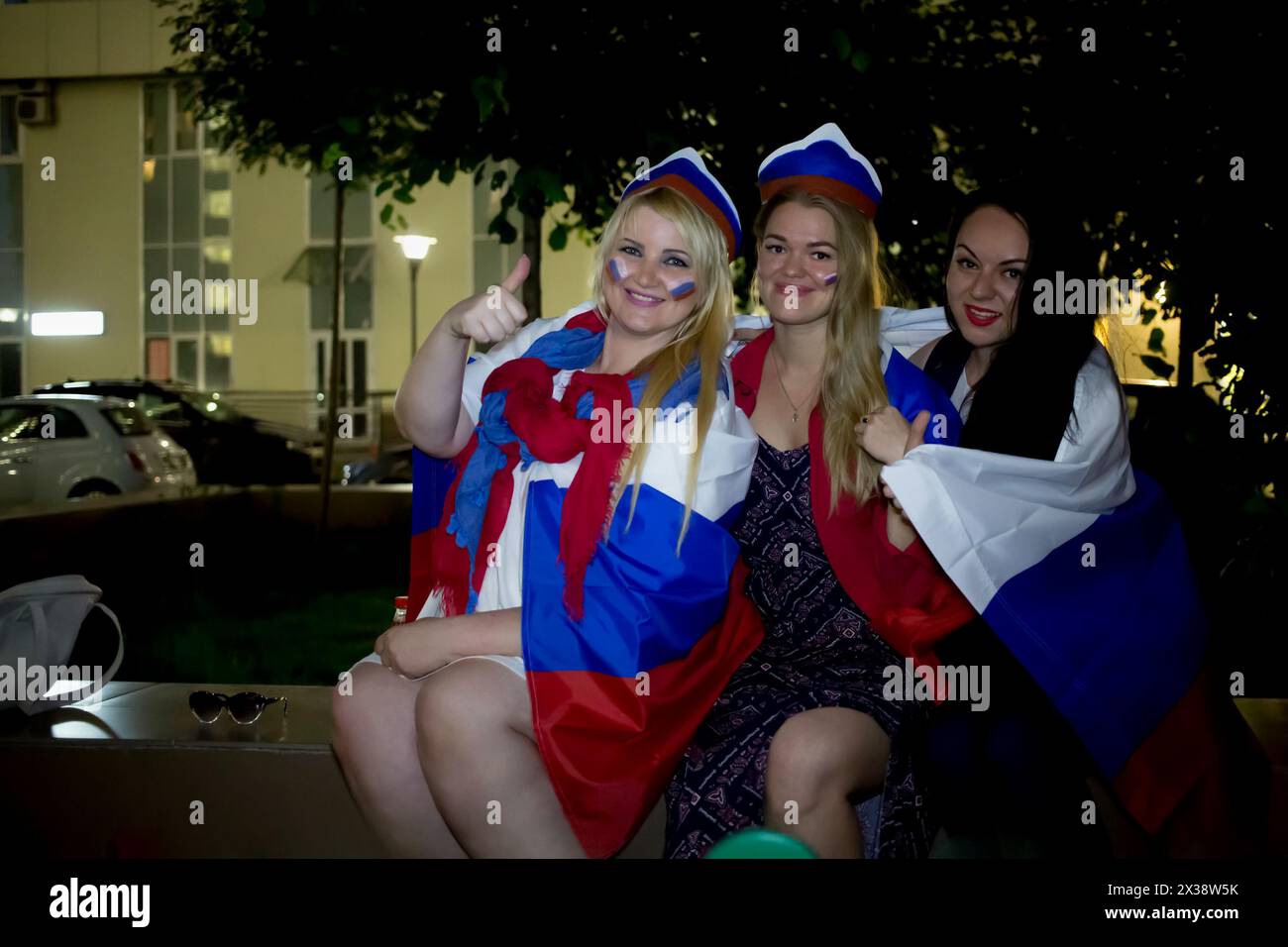 Three smiling women covered with Russia flag sit together outdoor in ...