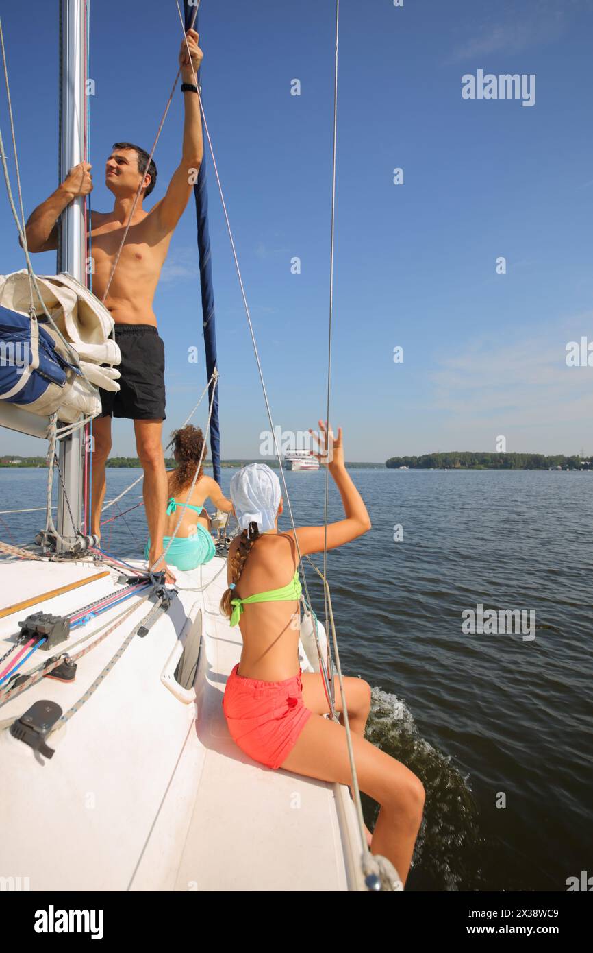 Father, mother and daughter sail on yacht on rive at summer, child waves hand for big ship Stock ...