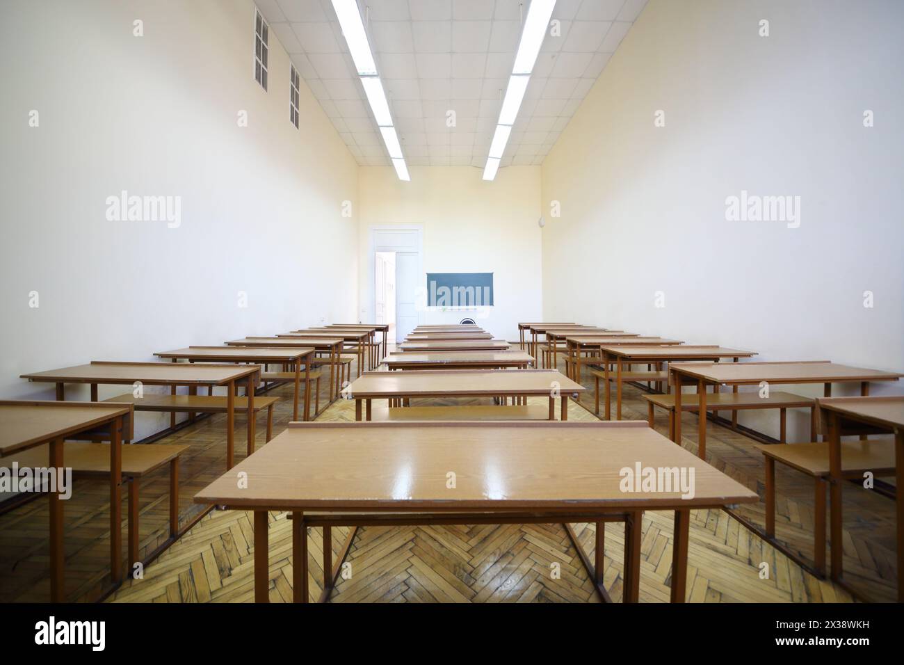 Lit classroom with rows of wooden tables for students and chalkboard ...