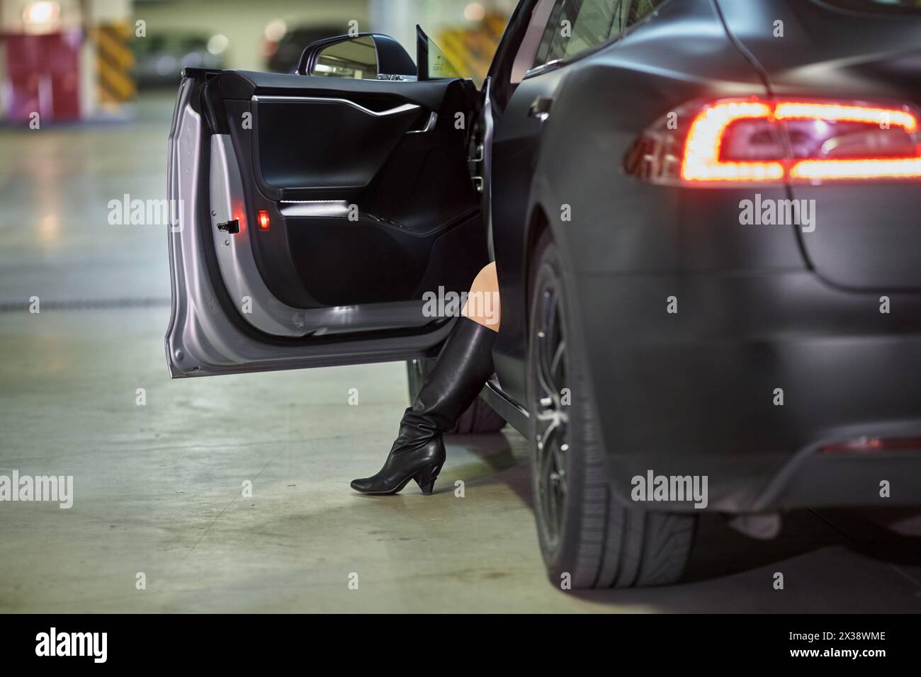Rear view of modern car with open driver door and leg of woman comes ...