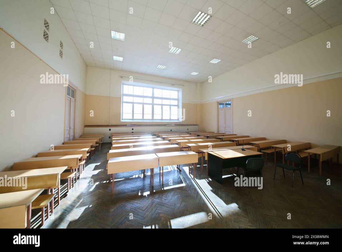 Sunny classroom with rows of wooden tables for students and big window ...
