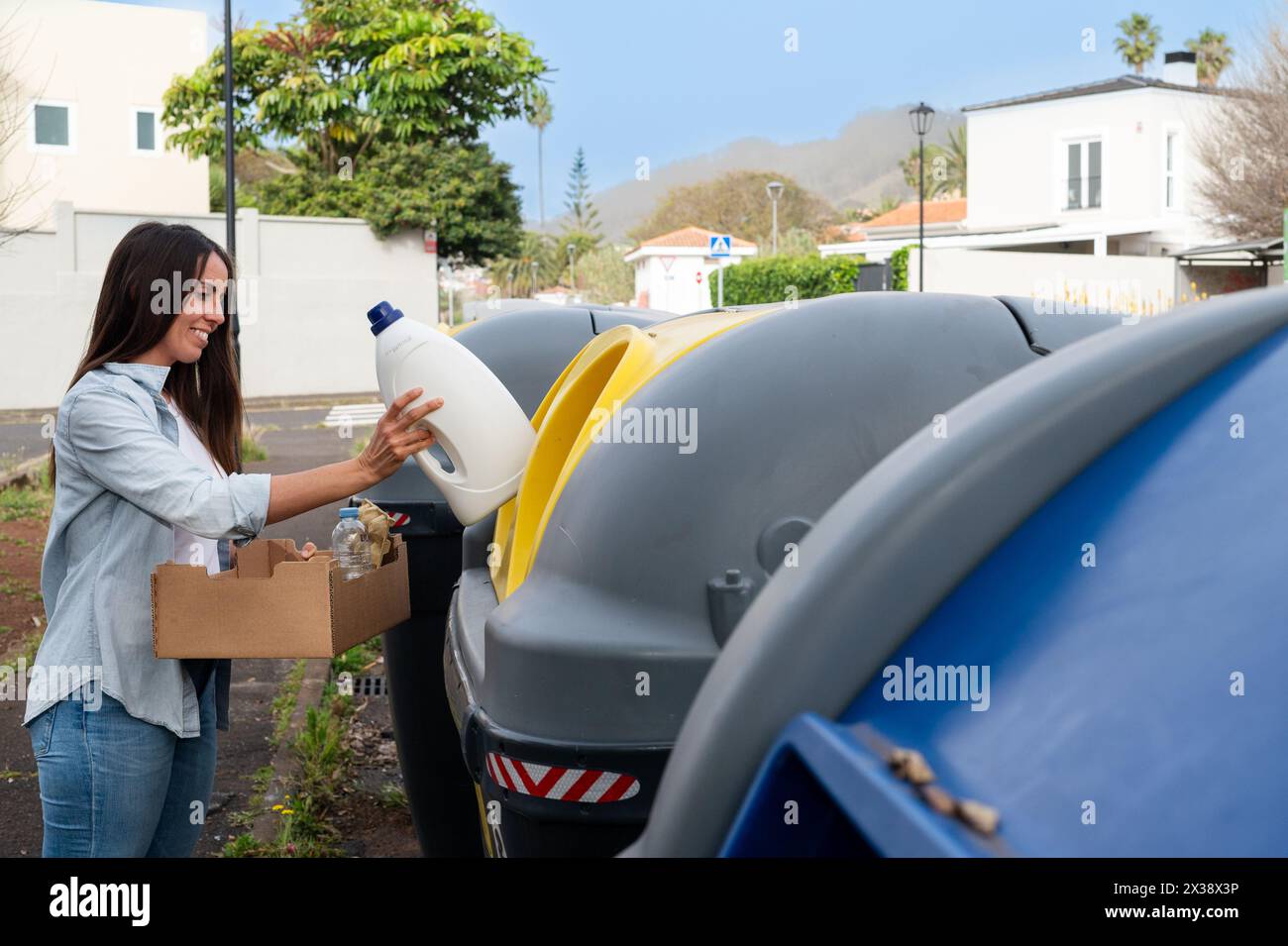 A woman smiles as she throws away a container in the recycling bin. The ...