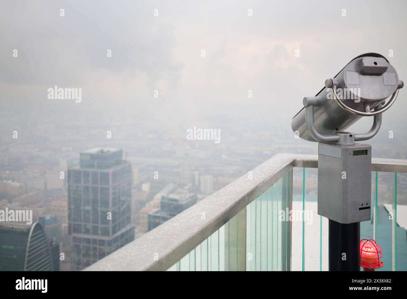 Binoculars on viewing platform on rainy day and office buildings in fog ...
