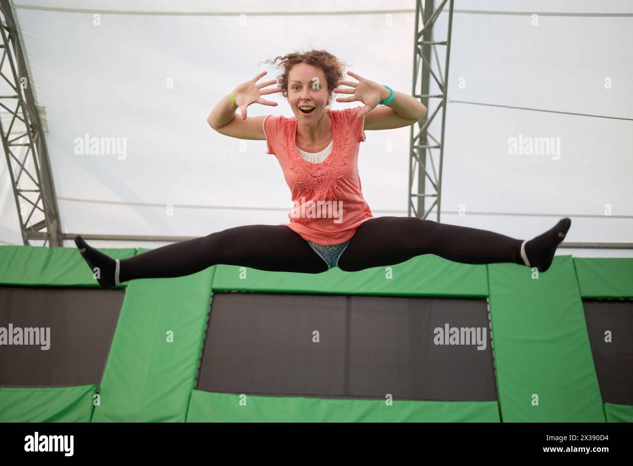 Young woman jumps on trampoline attraction making leg-split and ...