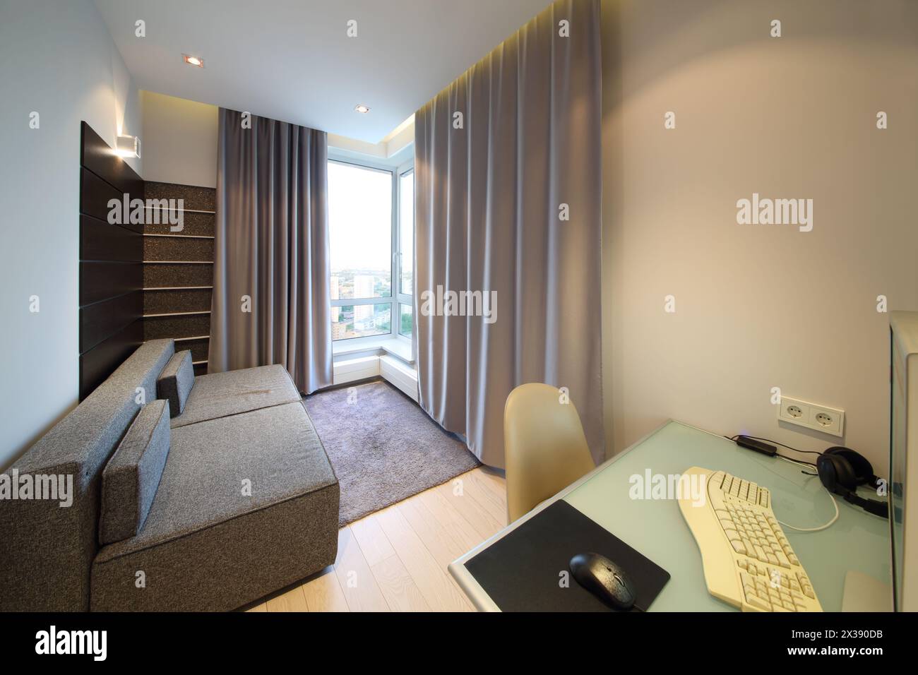 Sofa in front of a bay window with curtains and desk with a computer in ...