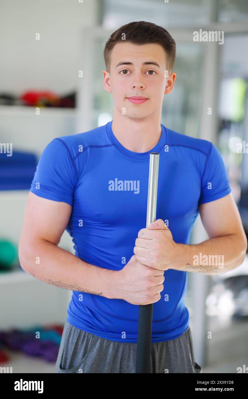 Young slim man stands with training pole in modern gym with fitness ...