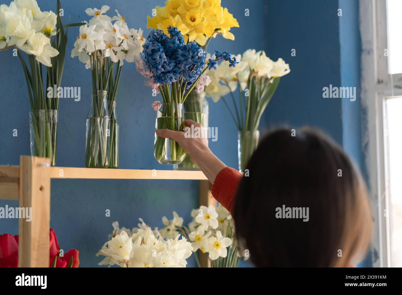 female florist placing a vase of flowers on a shelf while working in ...
