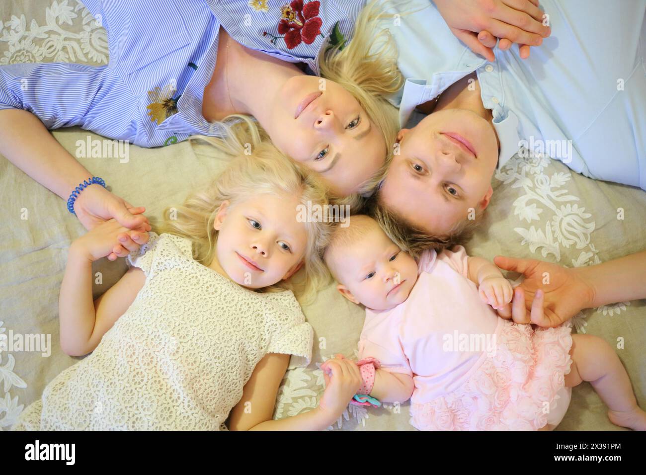 Mother, father, happy little daughter and baby lie on bed in room, top ...