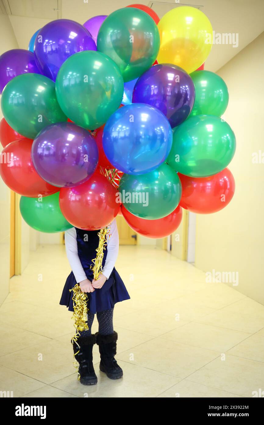 Pretty little girl hides behind many balloons in empty hallway of ...