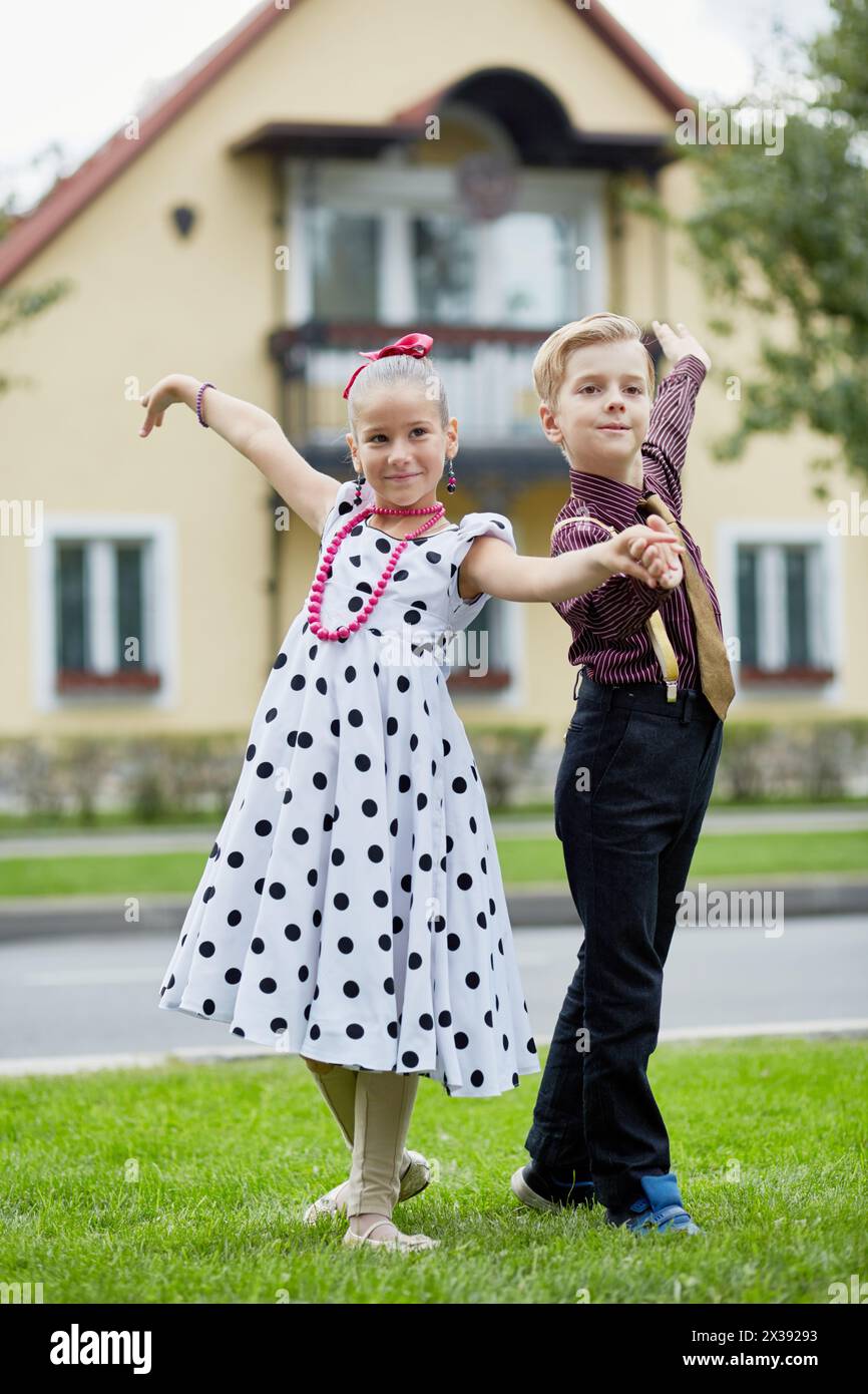 Boy and girl in dancing suits dance on grassy lawn against two-storied ...
