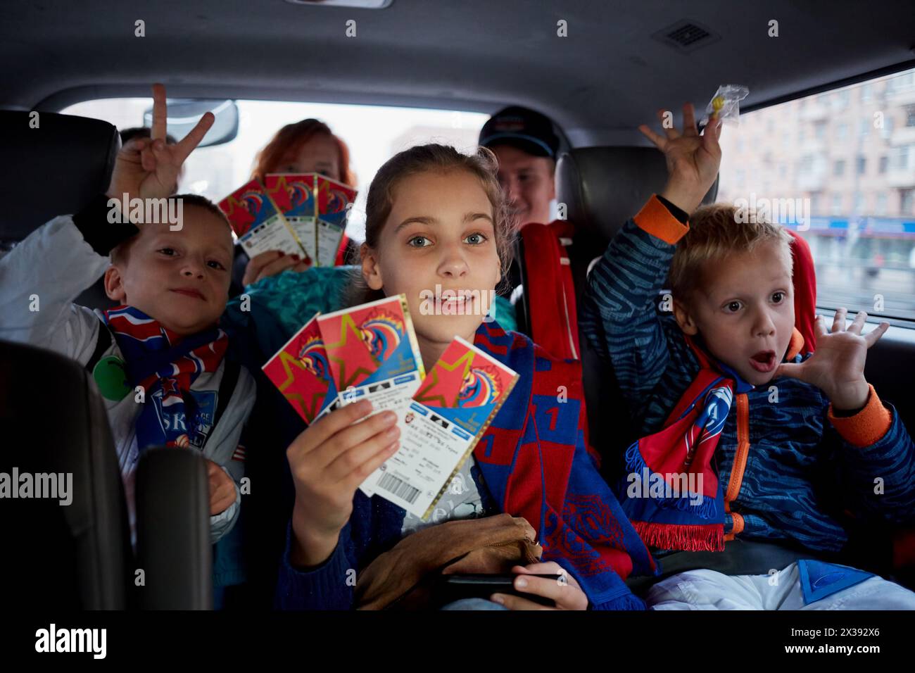 Three children and two adults in car cabin show tickets for soccer ...