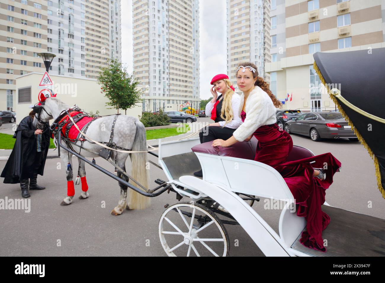 Woman in dress poses in coach with coachman girl near buildings, man ...