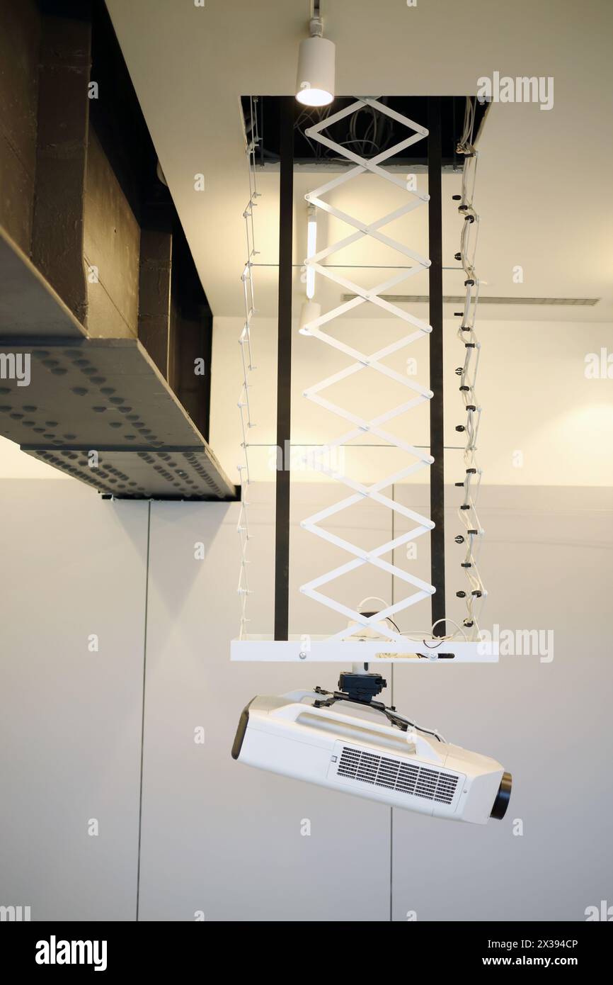 White modern projector for presentation hangs from ceiling in hall ...
