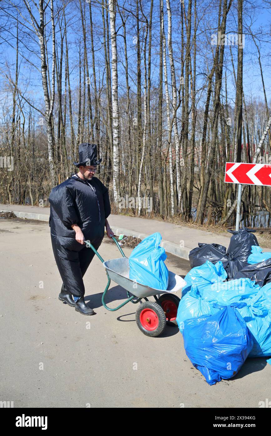Man in inflatable fat costume with wheelbarrow collects garbage in area ...