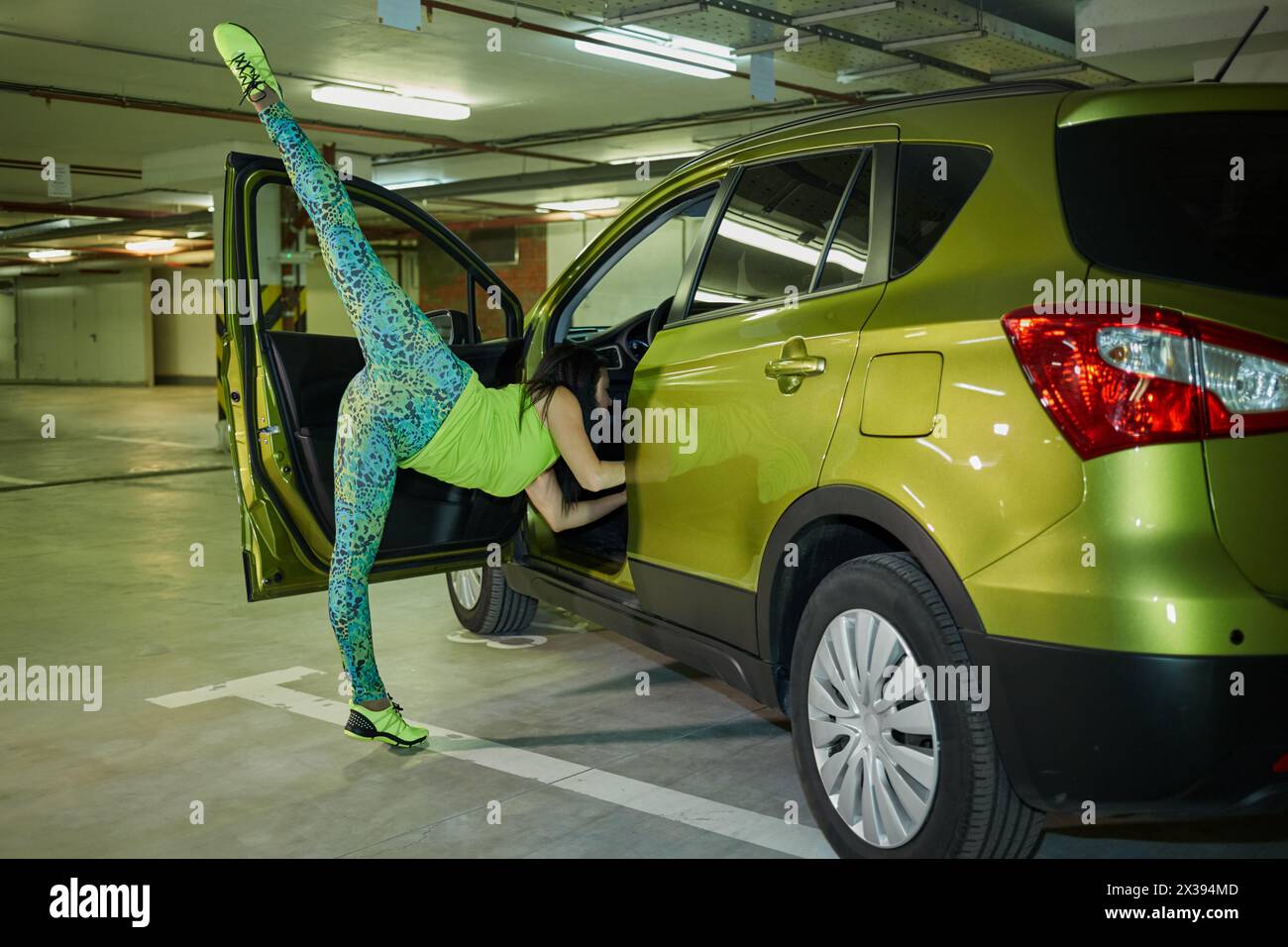 Young smiling woman does stretching exercise at car in underground ...