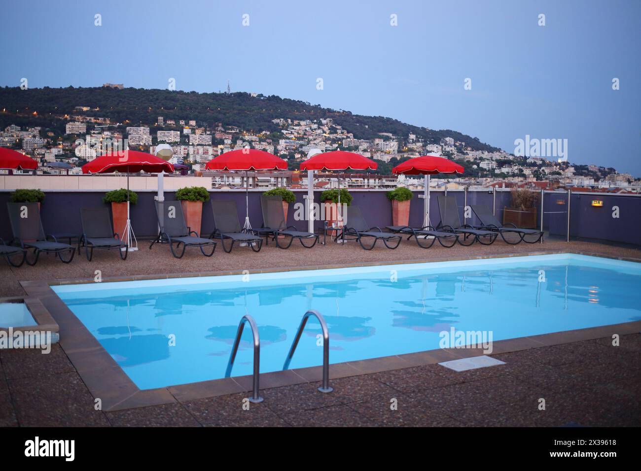 Empty small pool on rooftop, loungers, umbrellas at evening in town on ...