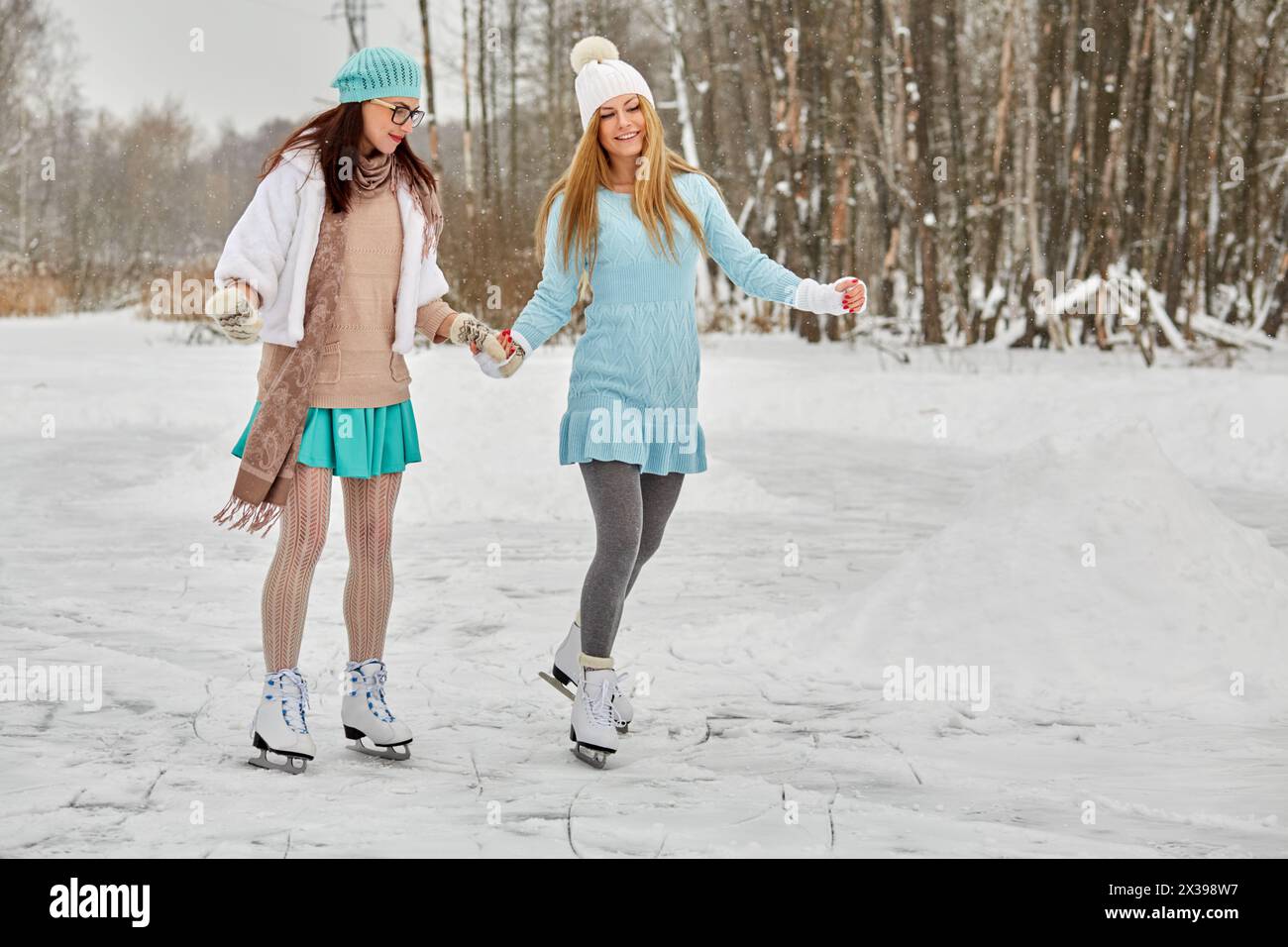 Two young women skate holding hands at outdoor skate rink in winter ...