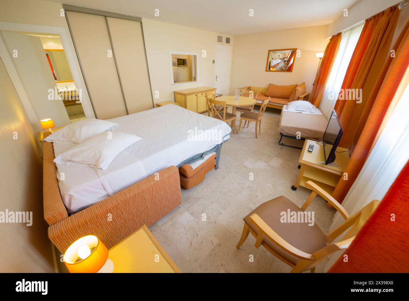 Empty hotel light room with white double bed, sofa and dining table ...