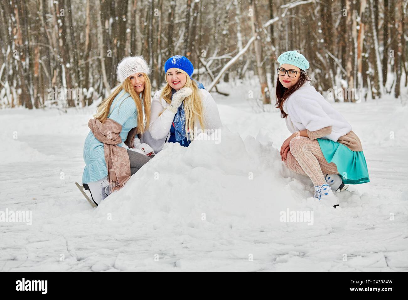 Three smiling women sit squatted near snowdrift at outdoor skate rink ...