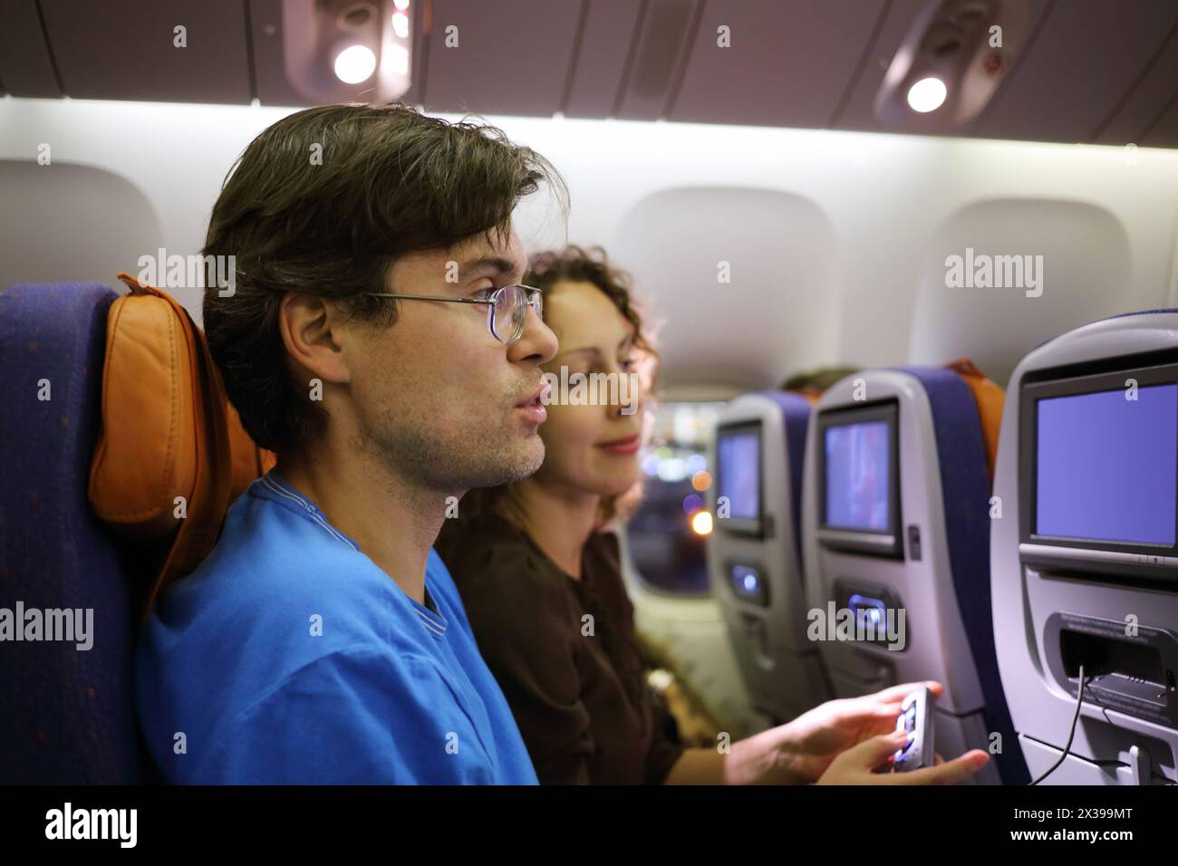 Man and woman switch channels on display on seat in airplane before ...