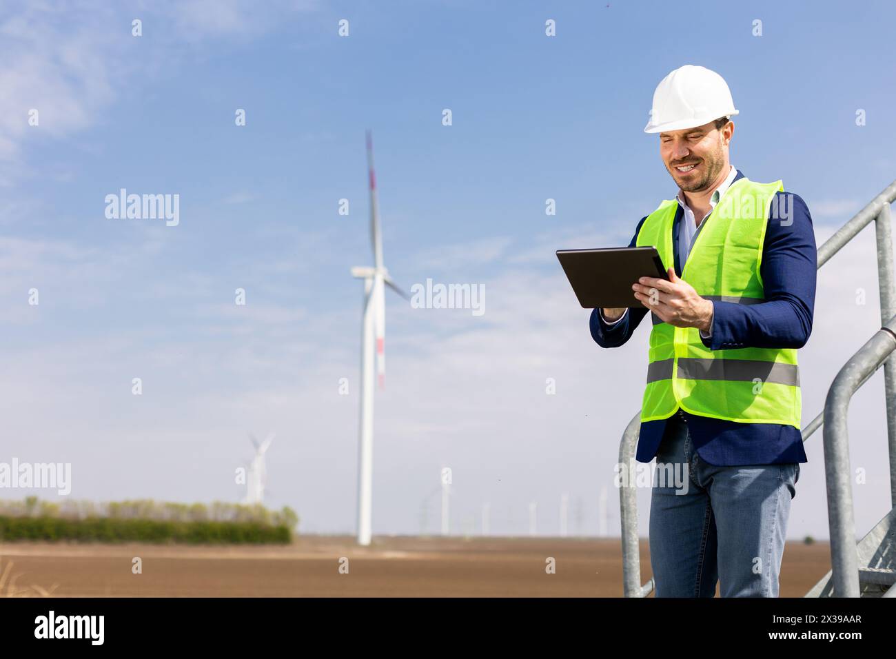 A cheerful engineer in safety gear reviews data on a tablet before ...