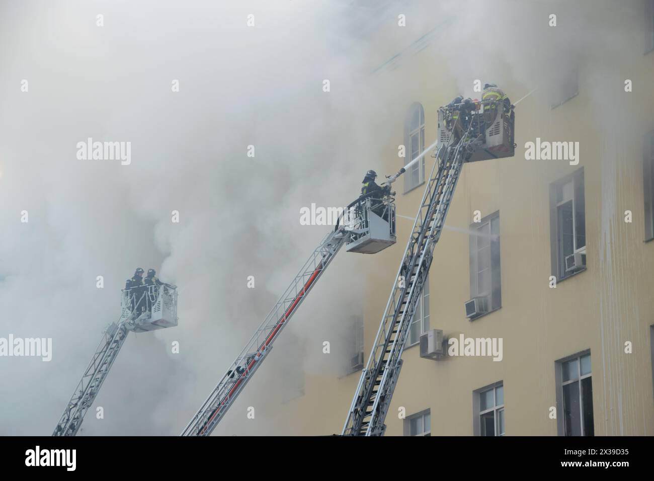 Firemen extinguish fire on fire trucks ladders - yellow building in ...