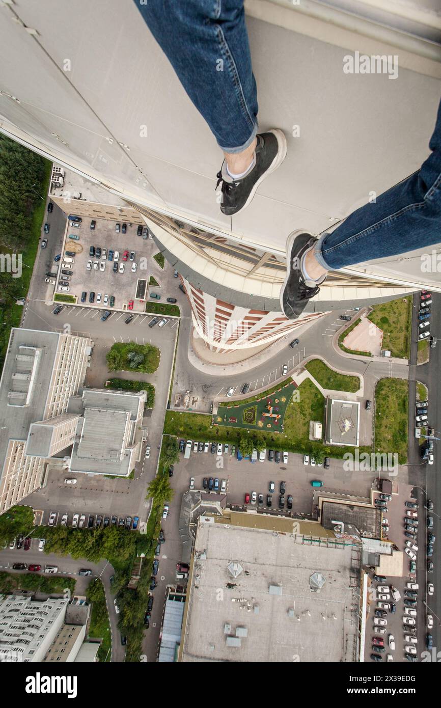 Legs of man in jeans sitting on roof of tall building at summer day in ...
