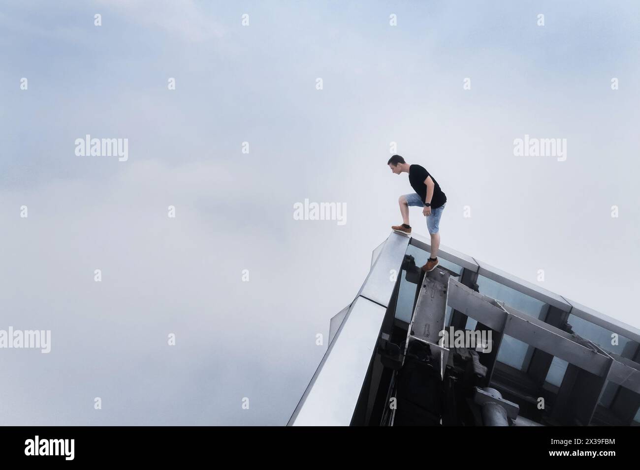 Man stands on rooftop of skyscraper among clouds and looks down ...
