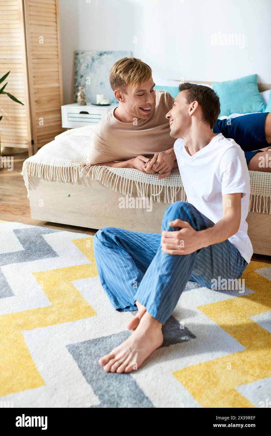 Two men in casual attire sitting close together on a bed Stock Photo ...