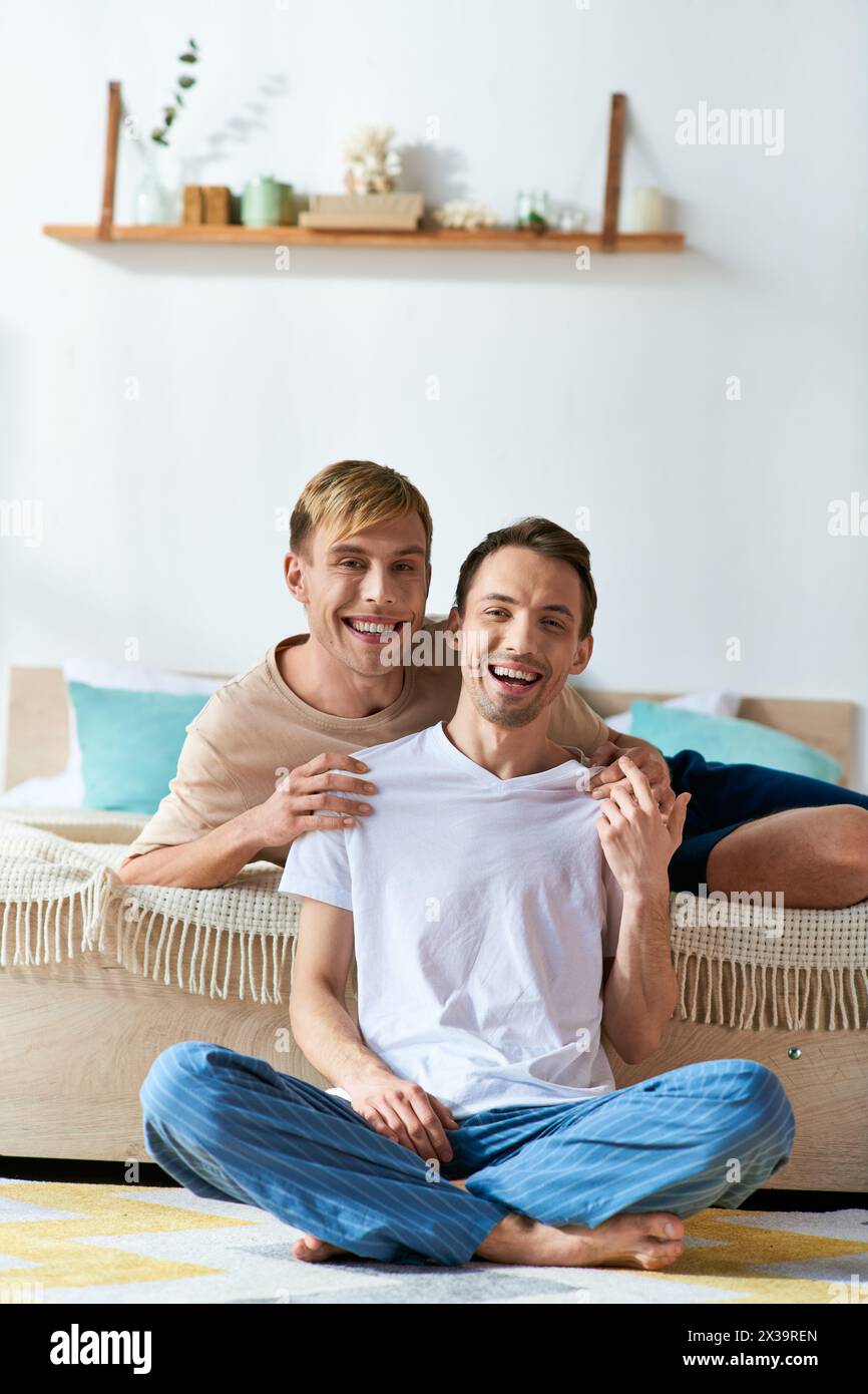 Two young men in casual attire sit on a bed, beaming with joy Stock ...