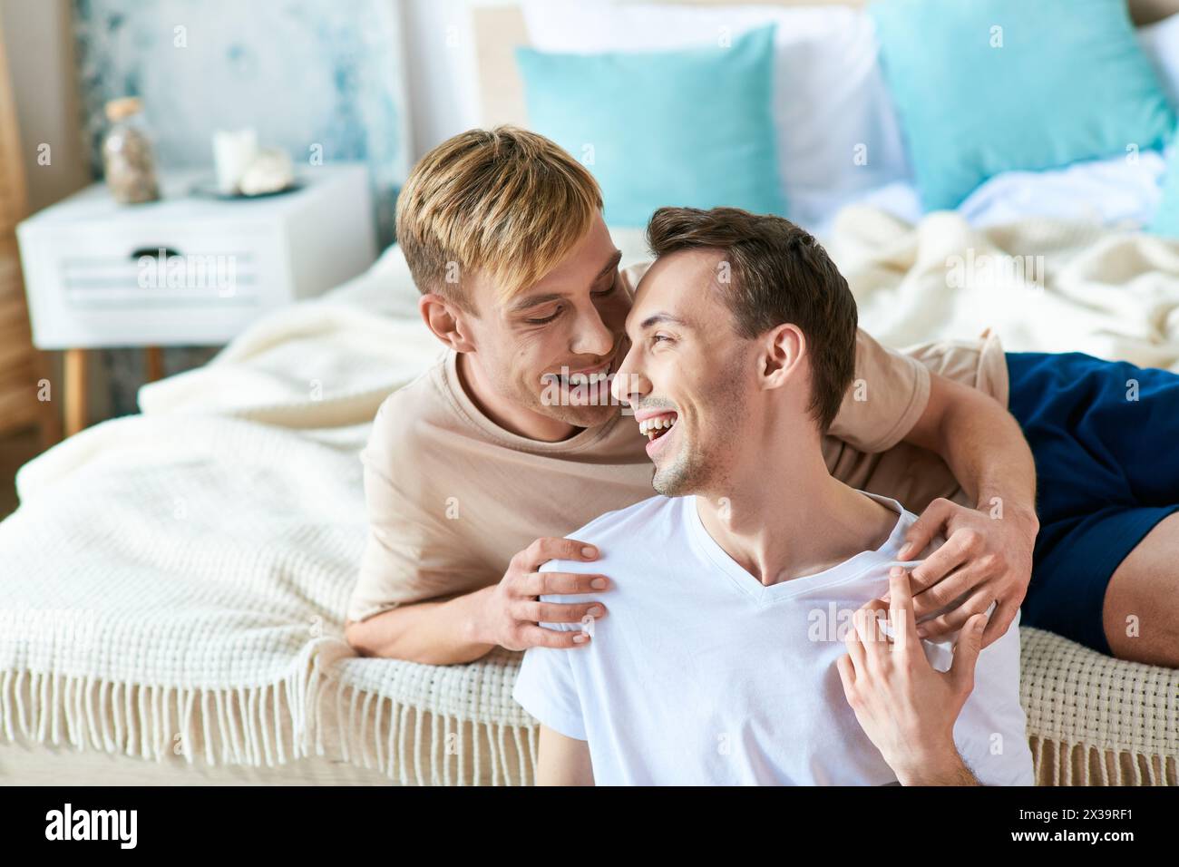 Two men in casual attire lie intertwined on a bed, exuding comfort and ...