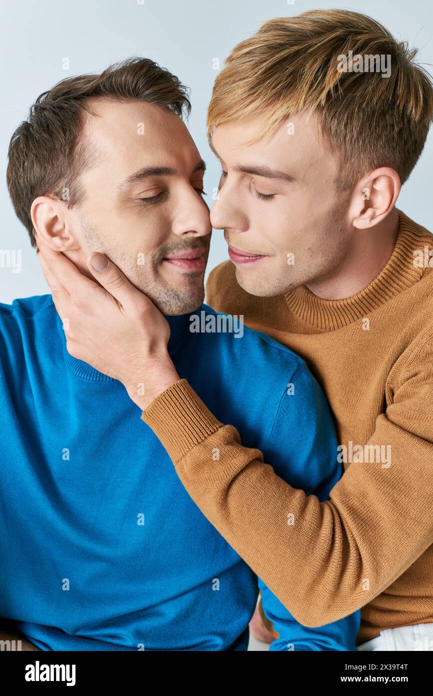 Two men in casual attire embracing each other tenderly against a gray ...