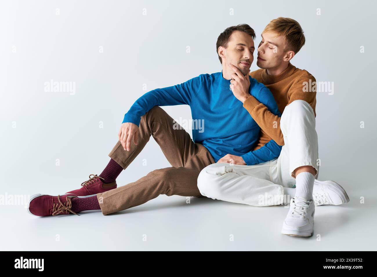 Two men in casual attires sit on the ground with their feet intertwined ...