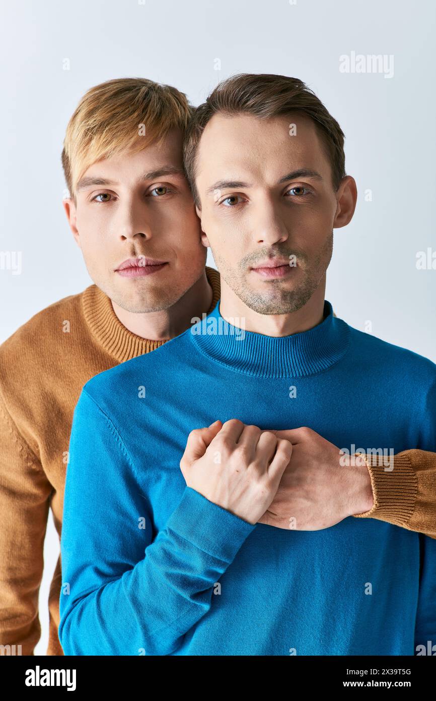 A loving gay couple in casual attire pose together on a gray backdrop ...