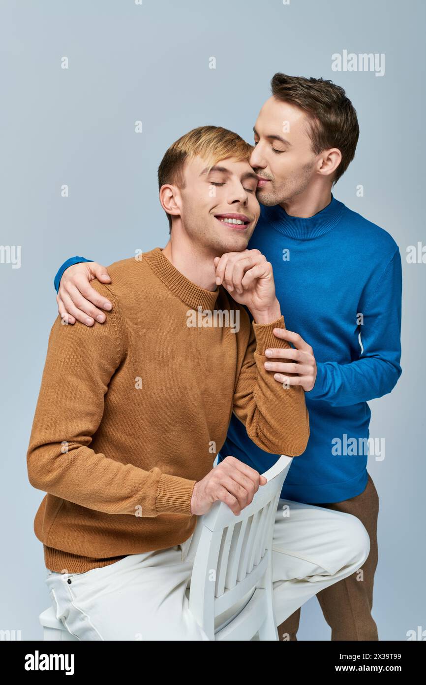 Two men in casual attires hug on a chair against a gray backdrop Stock ...