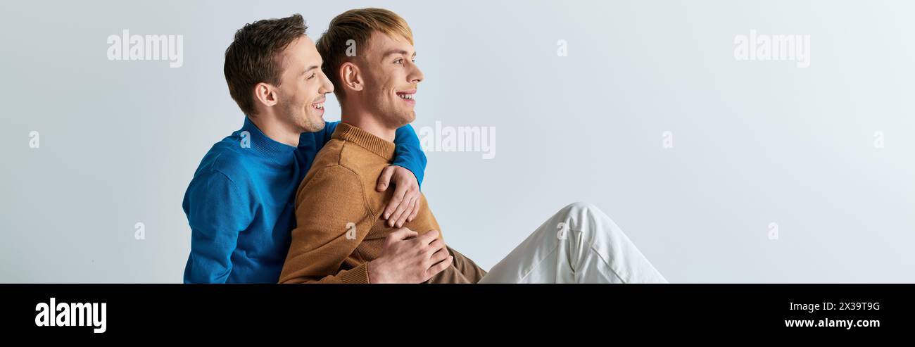 Two men in casual attire sitting lovingly intertwined on a gray ...