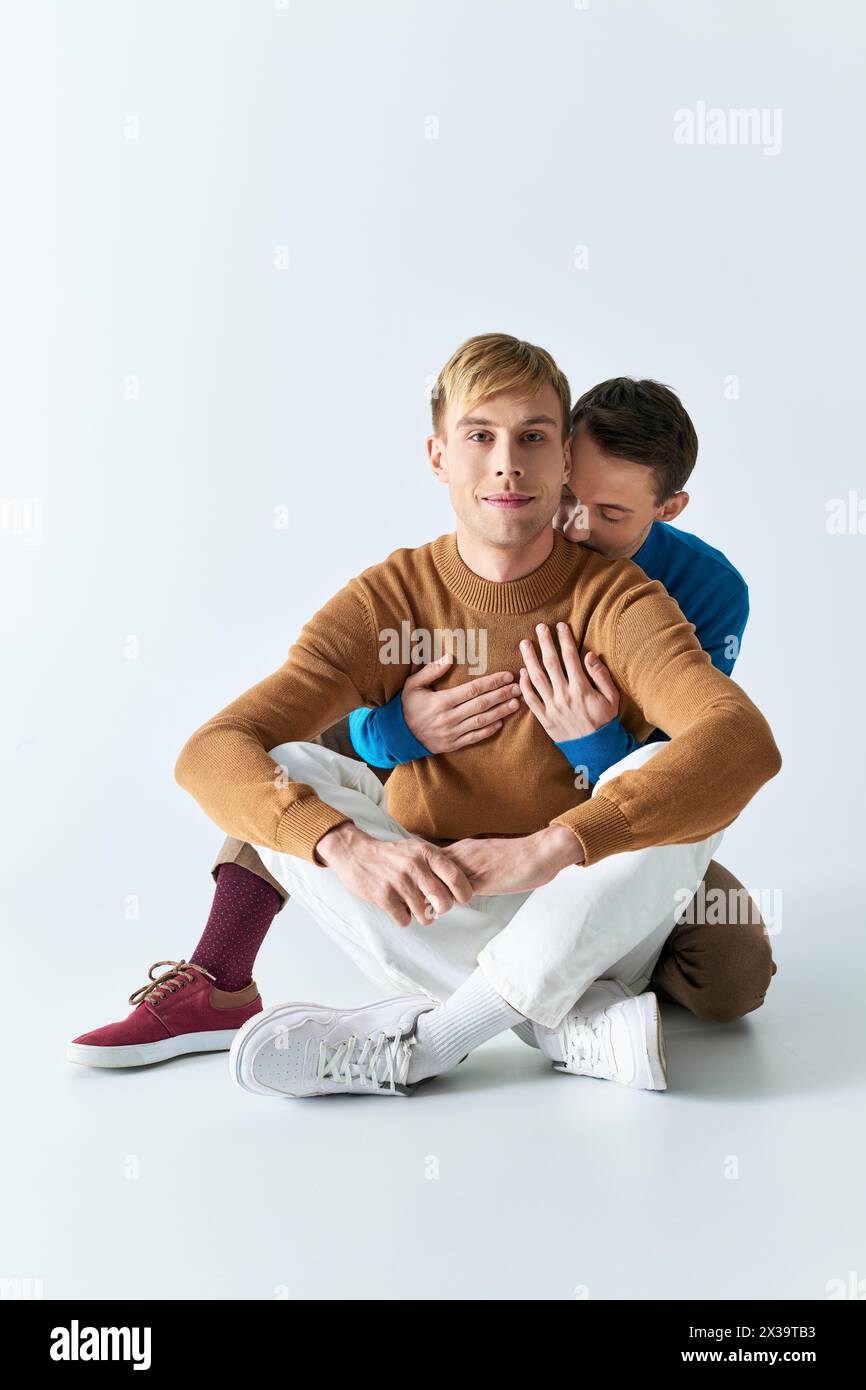 Two men sit closely, embracing each other with arms around, conveying ...