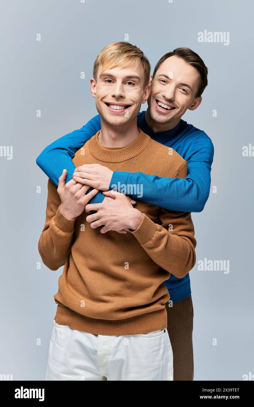 Two young men in casual attire hug each other affectionately against a ...