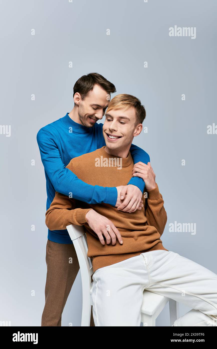 Two men sit on a chair, arms around each other, showcasing love and ...