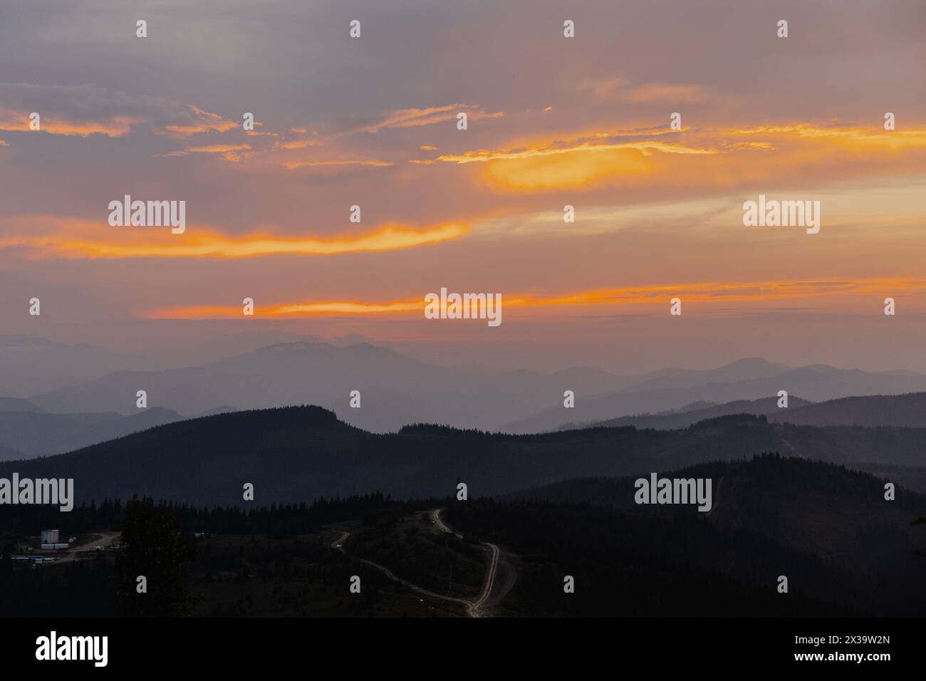 The sun setting behind a towering mountain range, casting long shadows ...