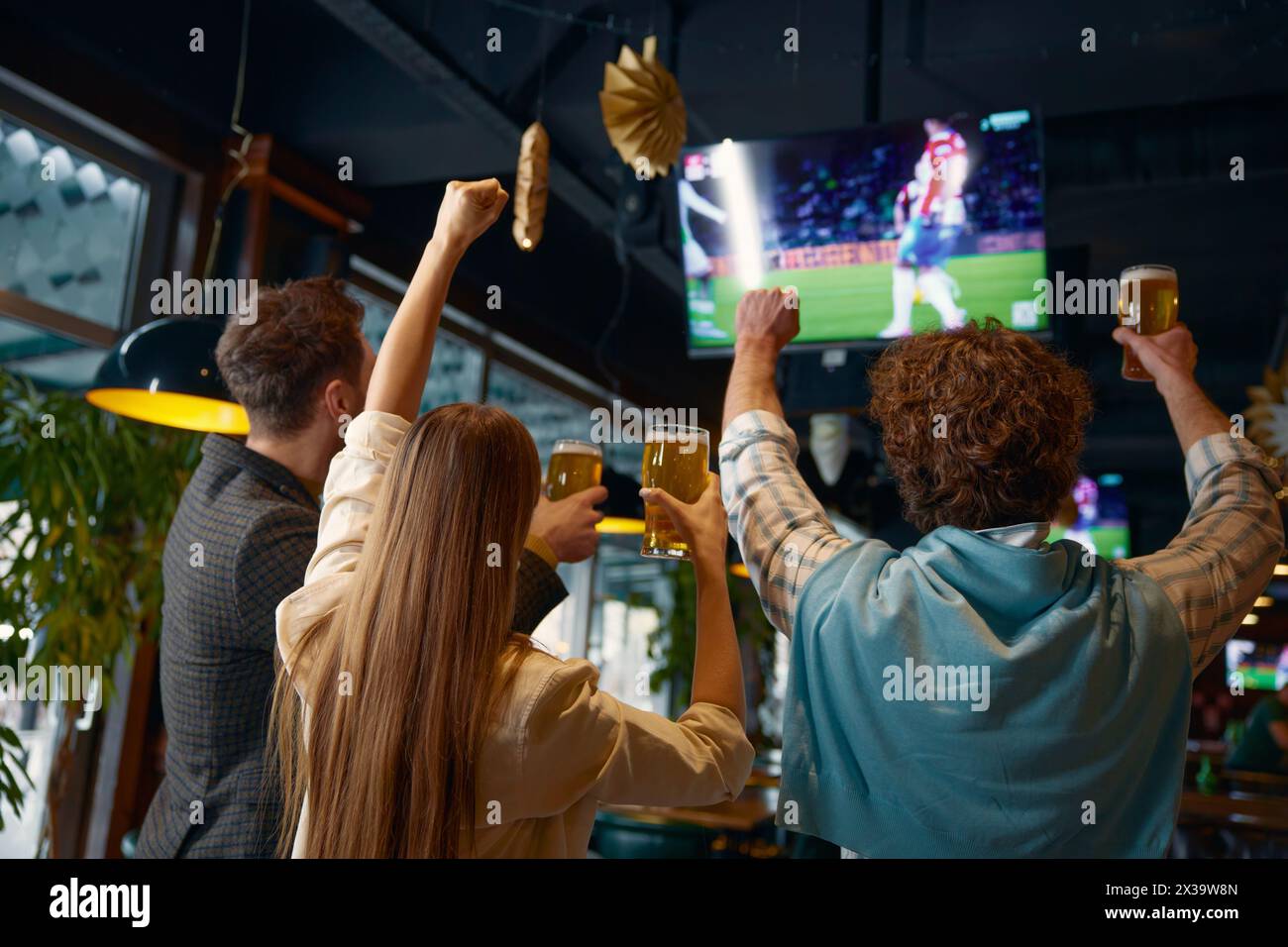 Happy excited group of friends watching football match on tv in pub ...