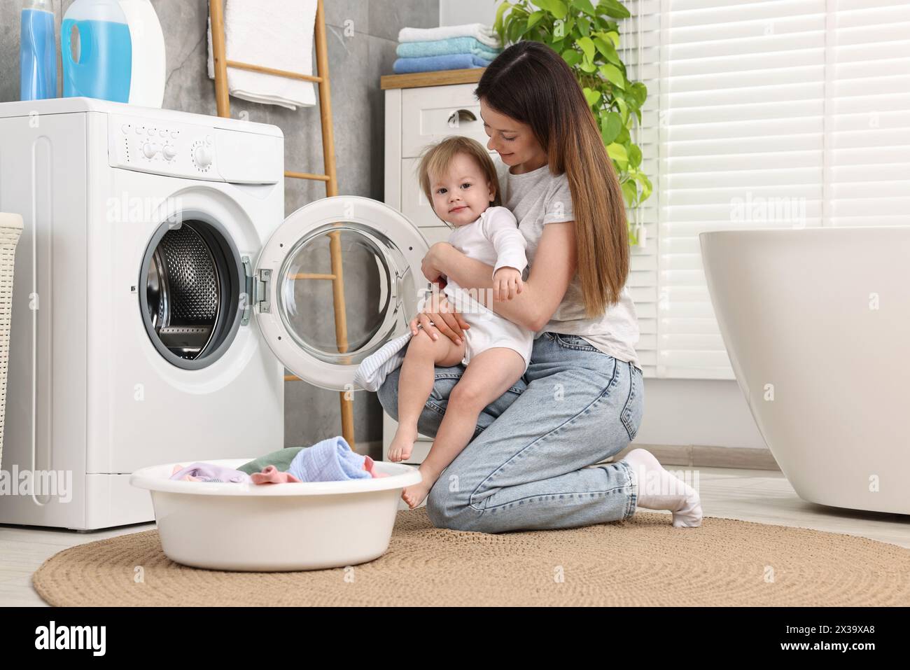 Mother with her daughter washing baby clothes in bathroom Stock Photo ...