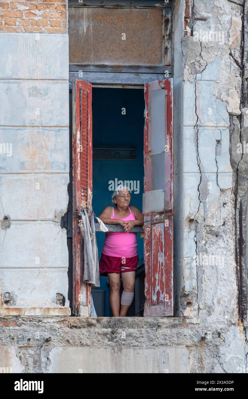 A woman looking out of her window, with its balcony fallen off, on a ...
